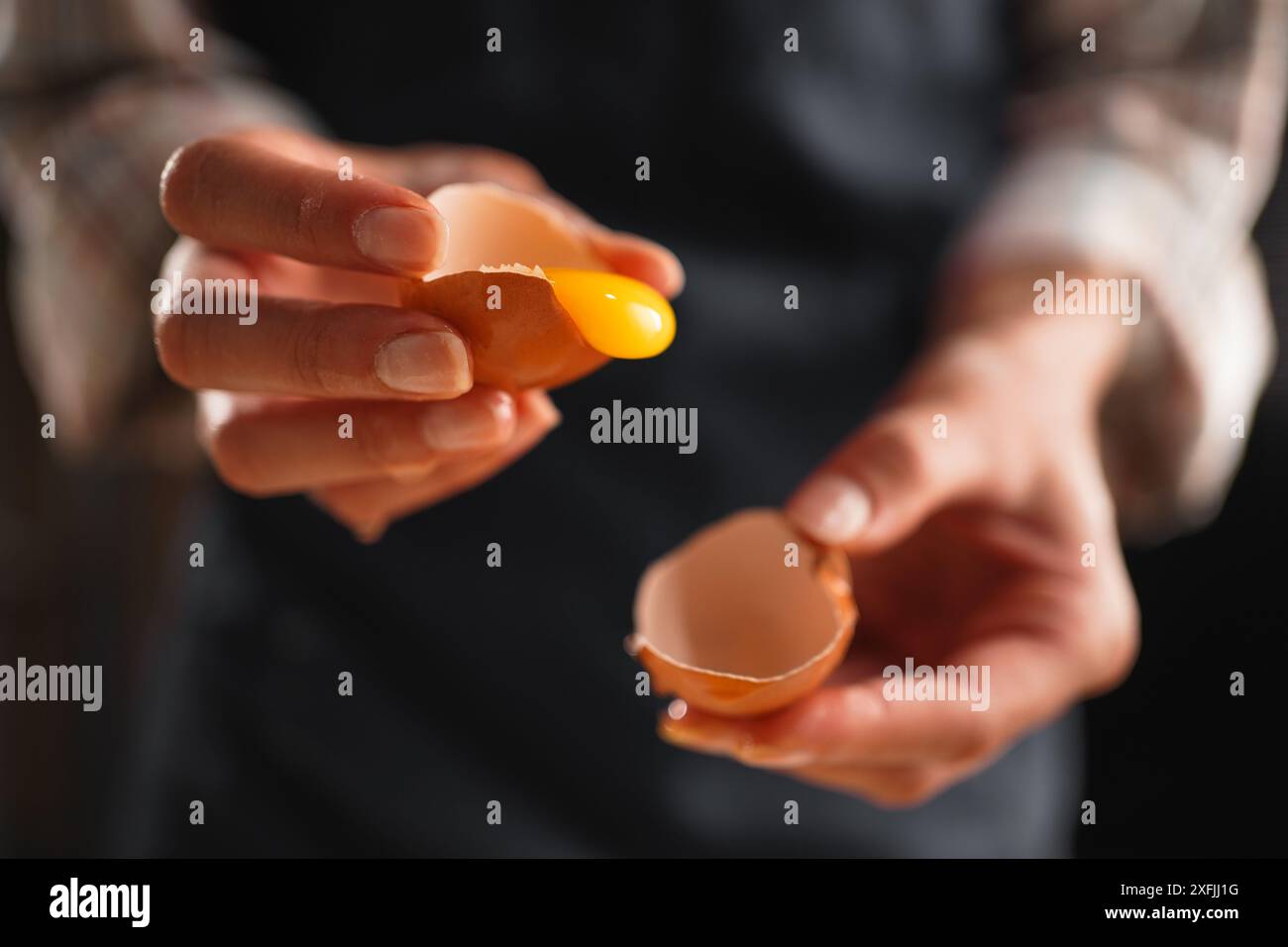 Female baker's hands cracking an egg with yolk dripping out, preparing ...