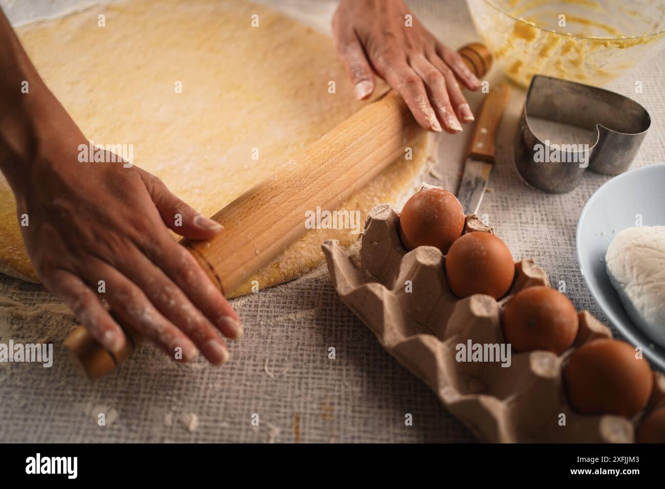 Baker's hands rolling out a sheet of dough using a wooden rolling pin ...
