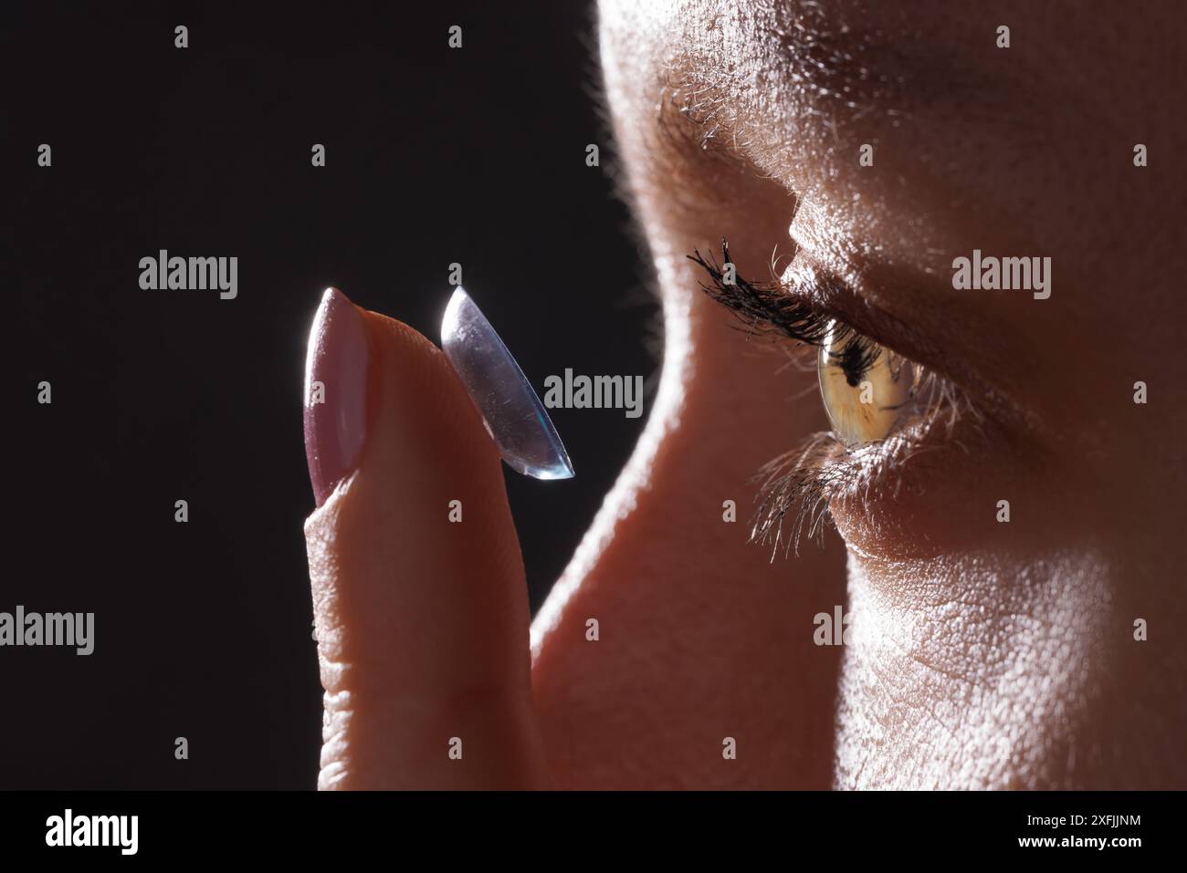 woman puts on contact lenses for vision close-up on a dark background ...