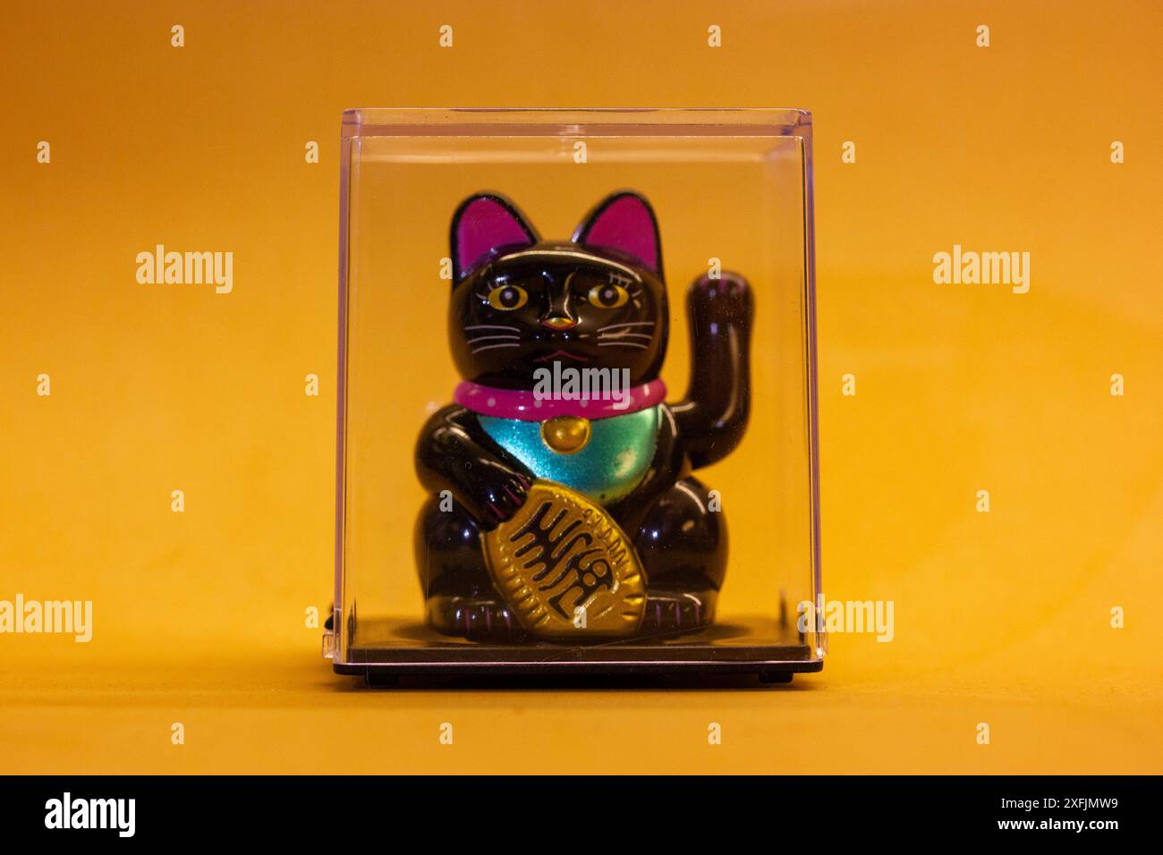Maneki Neko Japanese lucky cat waving a paw close up on yellow orange background. Chinese symbol ...