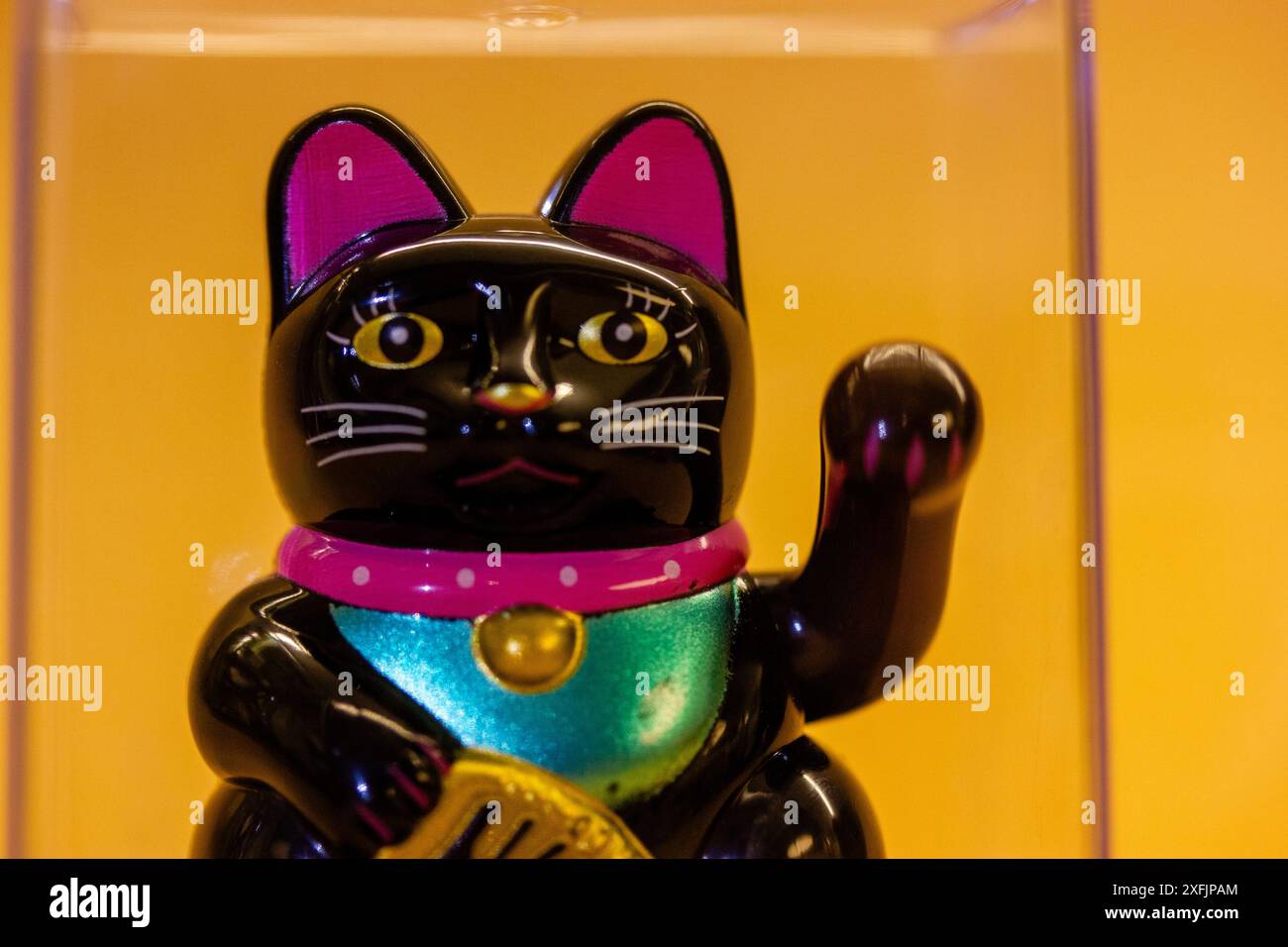 Maneki Neko Japanese lucky cat waving a paw close up on yellow orange background. Chinese symbol ...