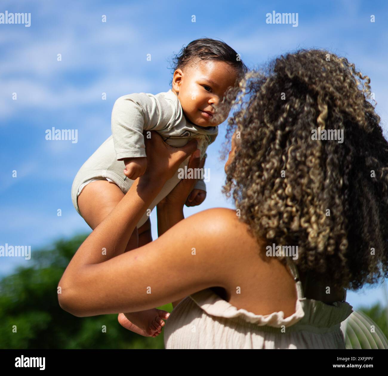 Latin mother with afro hair holding her 6 months old baby with blue sky ...