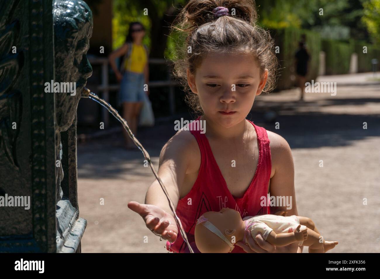 Little girl cooling off in a fountain with her toy on a hot day. Close ...