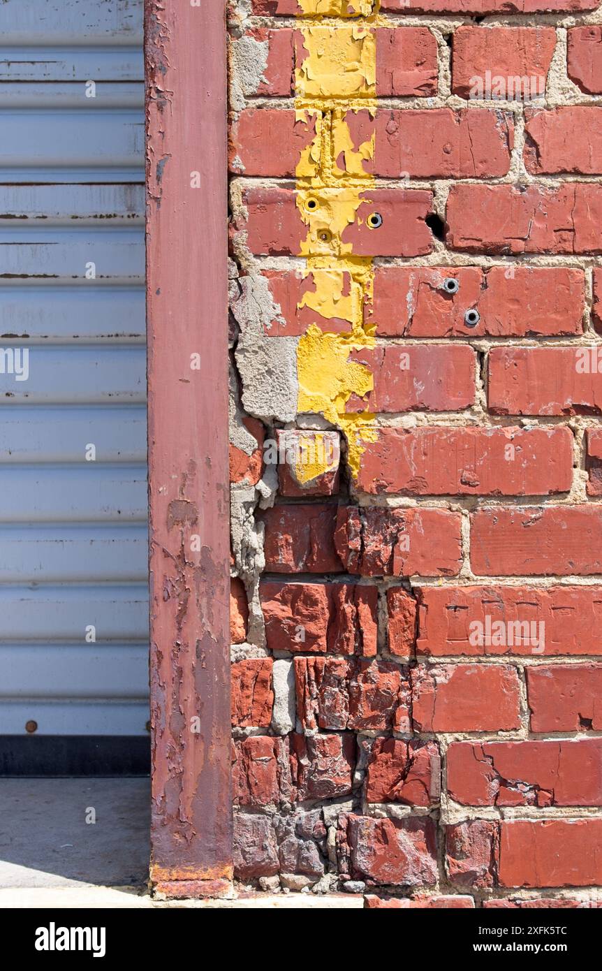 Damaged brick wall with yellow paint next to metal roll up door Stock ...