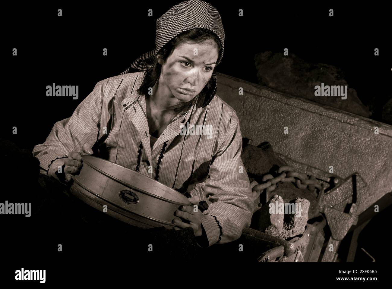Young woman sifting mineral inside an iron mine, done in sepia tone ...