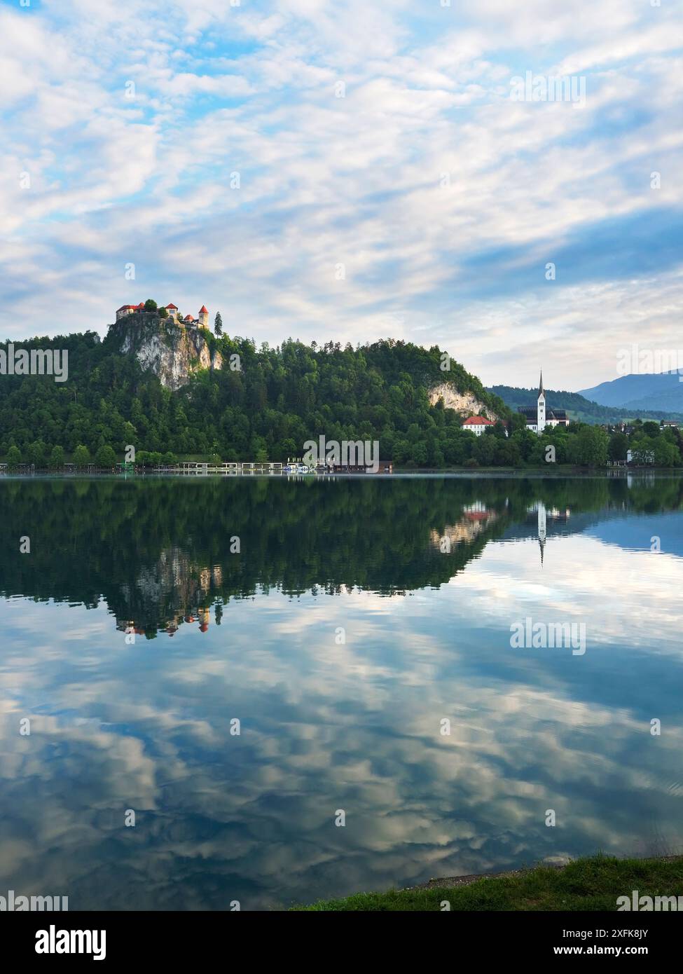 Bled Castle on cliffs reflected in Lake Bled early on a summer morning ...