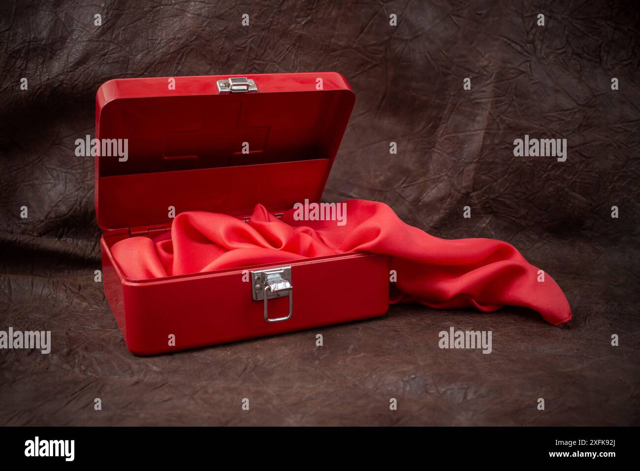 Red first aid kit box, opened with red satin fabric folds on brown ...