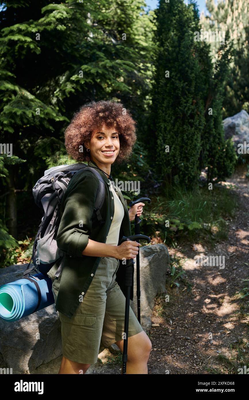A woman smiles as she hikes through a lush green forest, her backpack ...