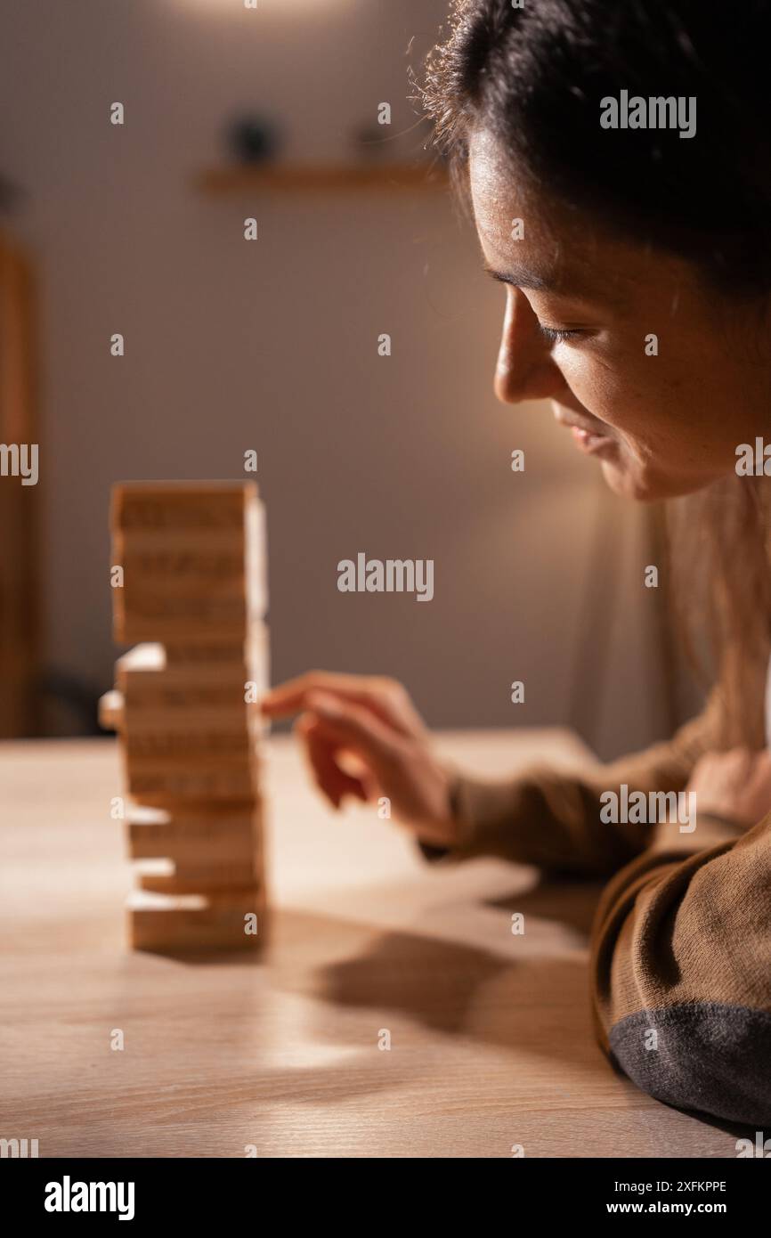 Woman playing wooden block game, carefully removing piece from tower ...