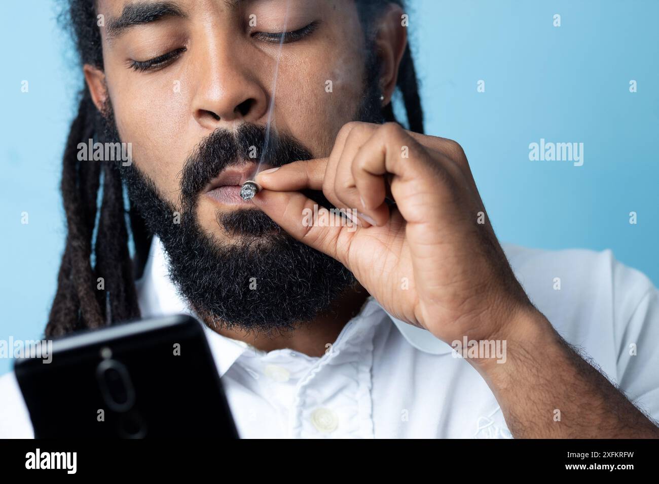 Black man with dreadlocks and black beard smoking weed holding the cell ...