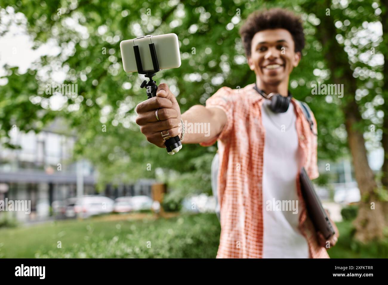 A young man, African American, snapping a selfie in the park with his ...