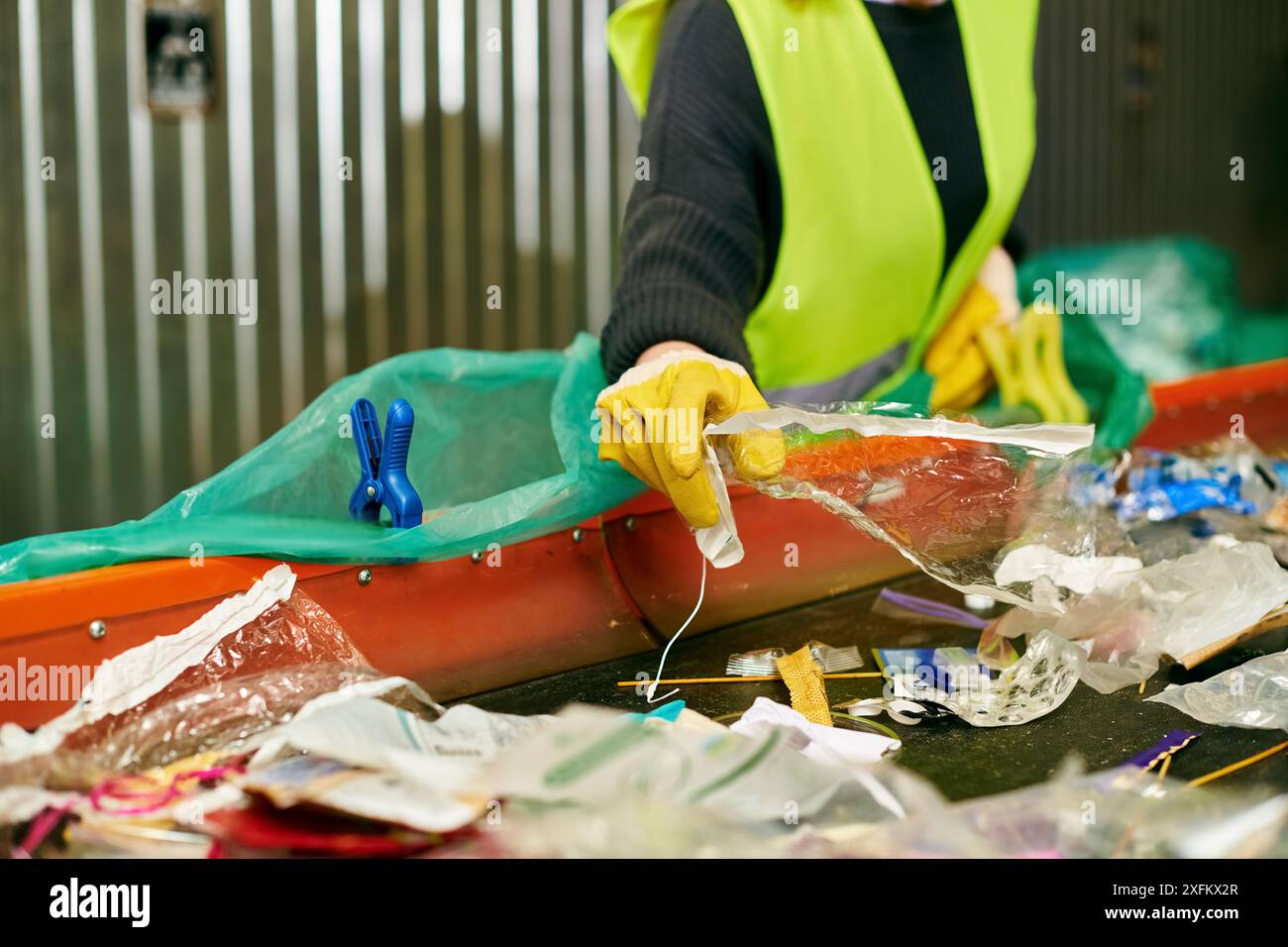 A young volunteer in a safety vest and yellow gloves sorts trash with ...