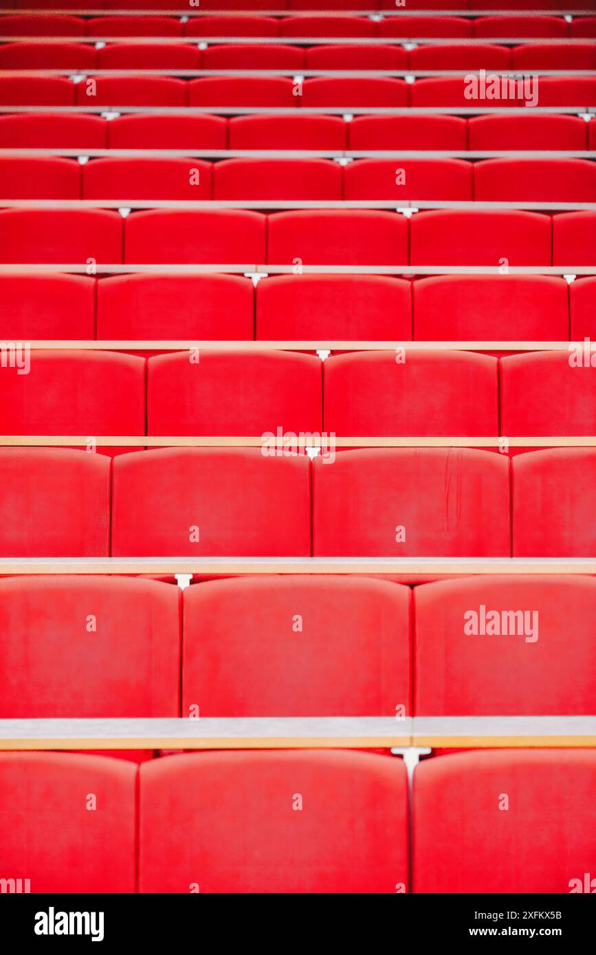 An empty auditorium or lecture hall, showcasing rows of red seats. The seats are empty, creating ...