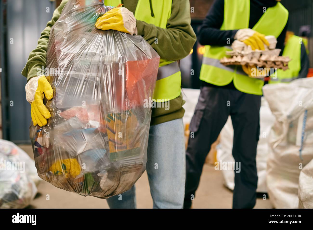 Two young volunteers in safety vests, gloves, and holding a huge bag of ...