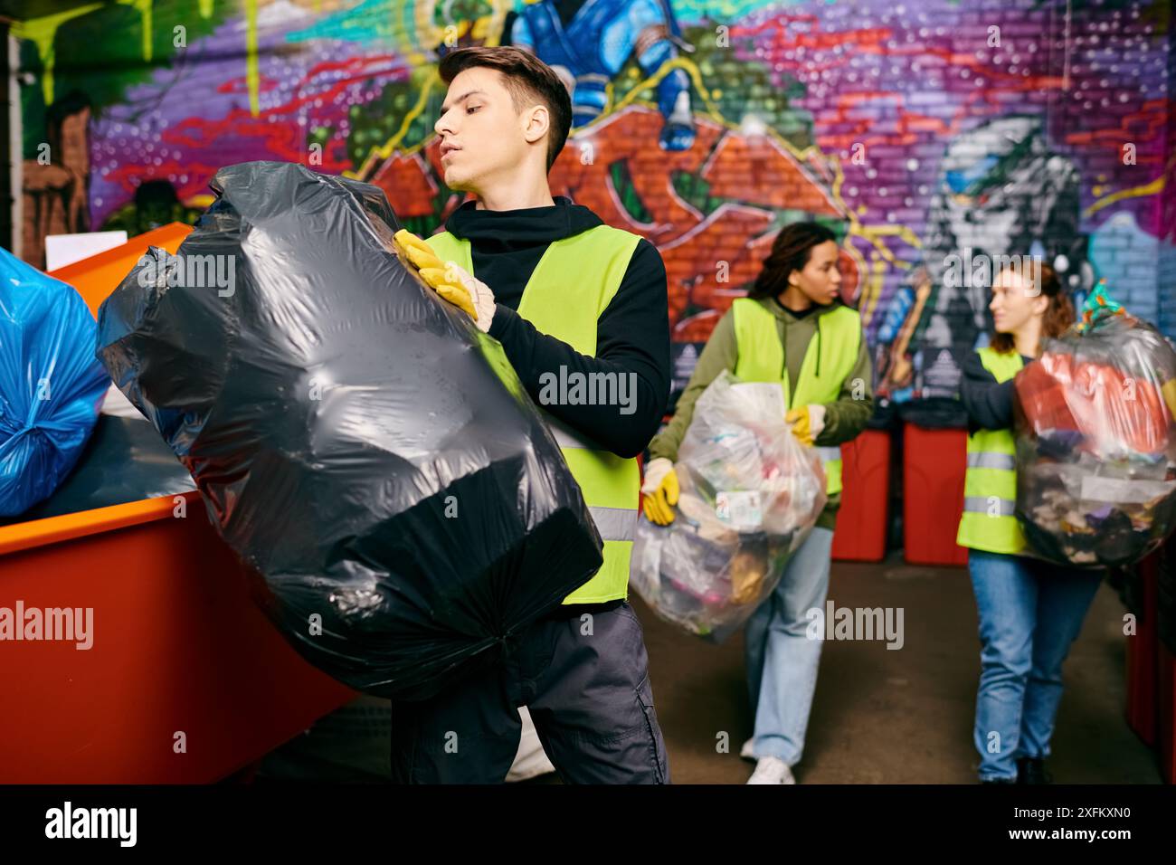Young volunteers in gloves and safety vests sorting trash in a room ...