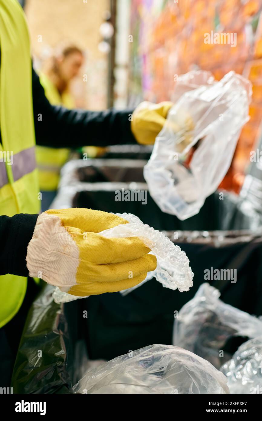 A young volunteer in a yellow safety vest and gloves sorting trash ...