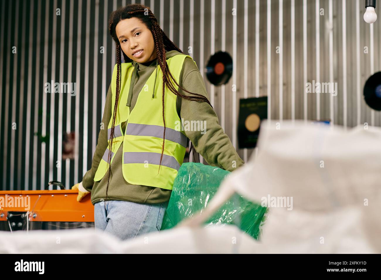 A young volunteer in a safety vest stands next to a pile of plastic ...