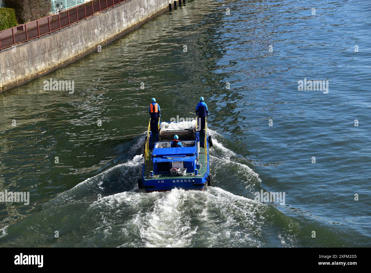 Three Japanese men steering a small garbage collecting boat in the Neya ...