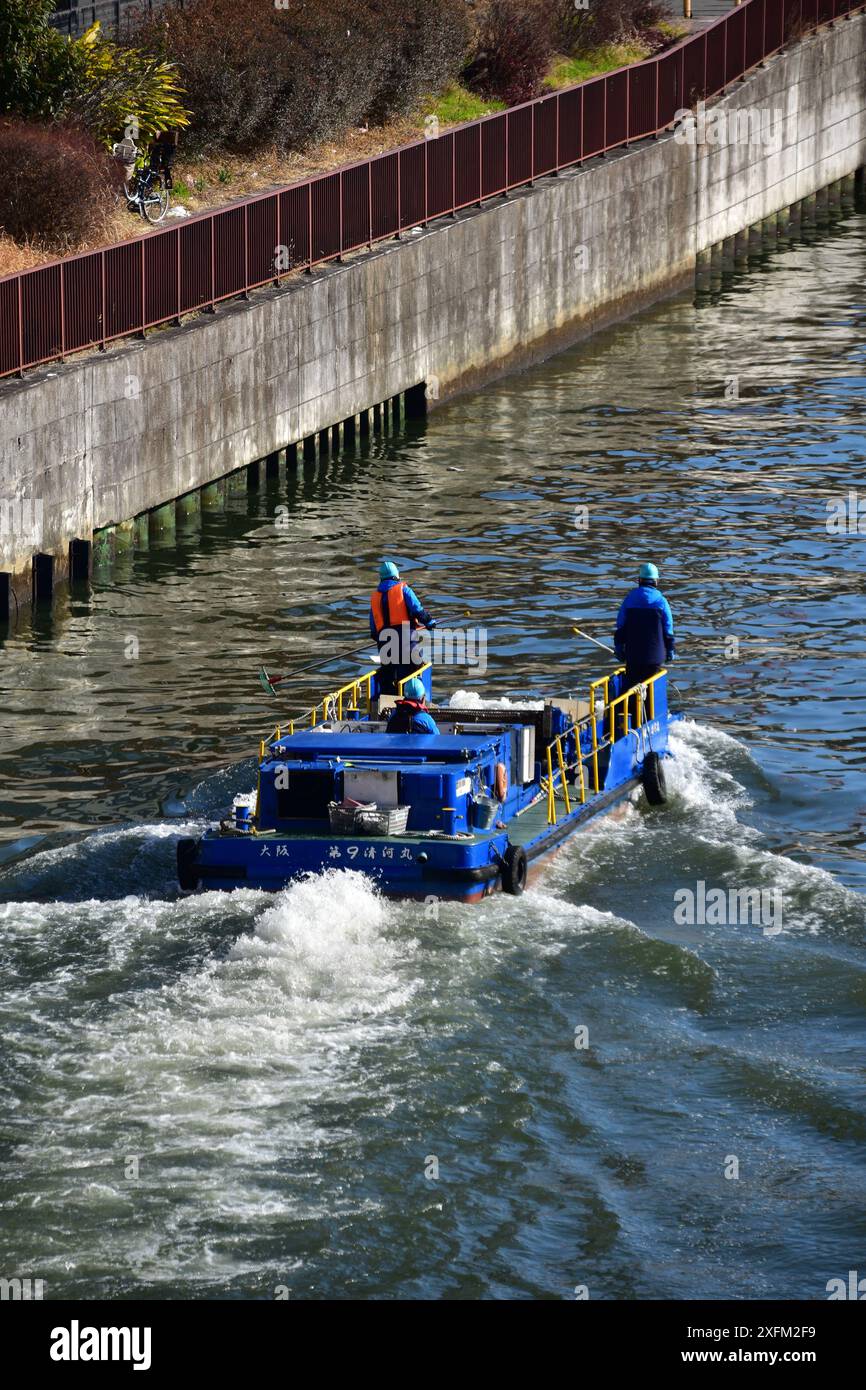 Three Japanese men steering a small garbage collecting boat in the Neya ...