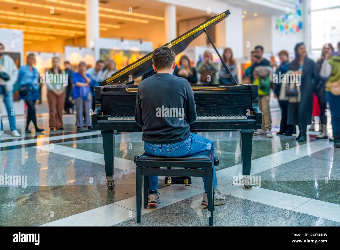 Rear back view of a man playing the piano in a public place and blurred ...