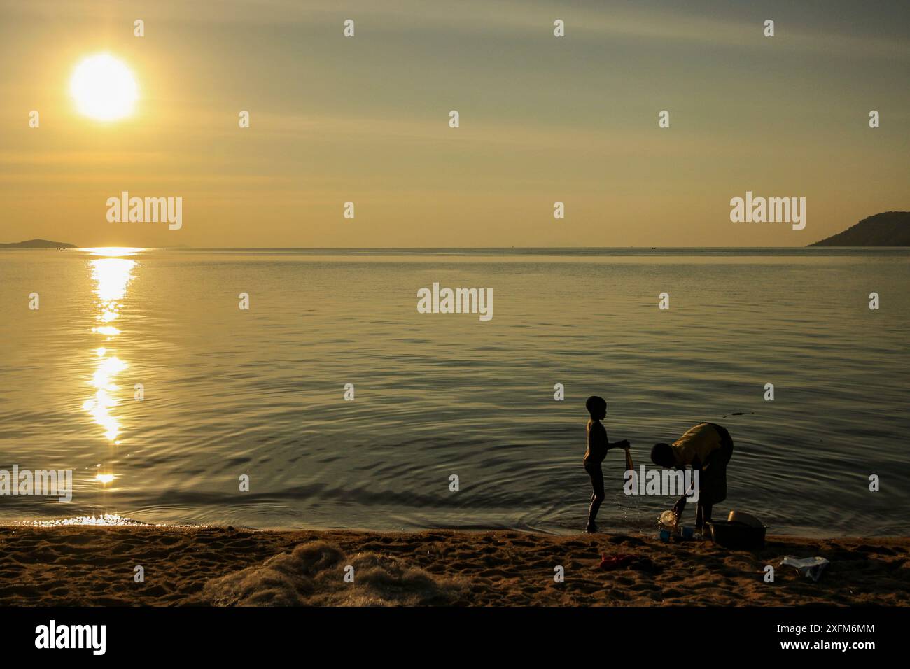 Woman and boy wash their clothes in Lake Malawi, at sunset, Cape ...