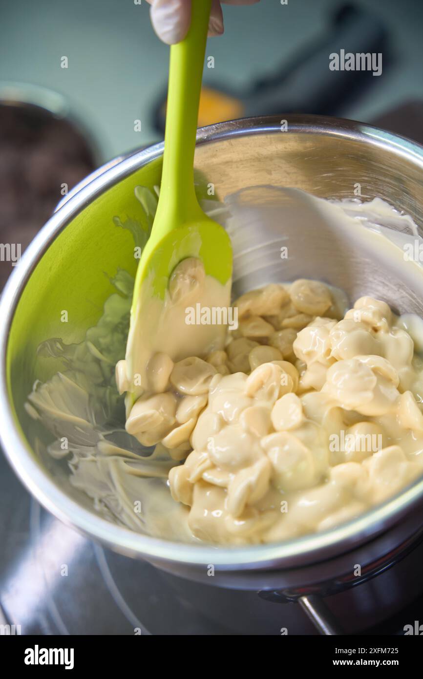 Person stirring white chocolate chips that slowly melting on steam bath ...