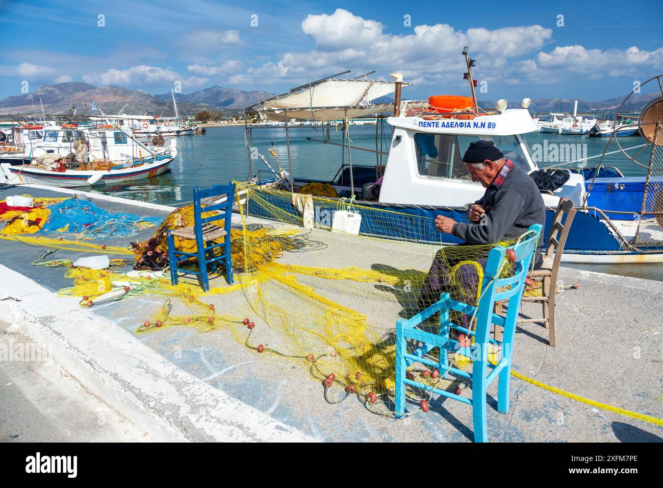 An old Caucasian fisherman untangles his nets at the small fishing port ...