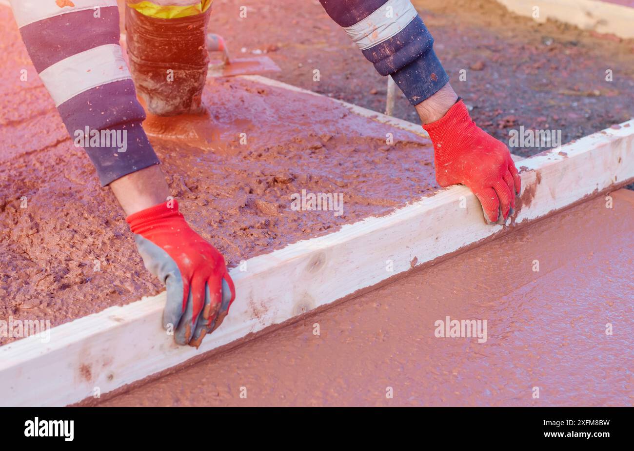 Builders pouring and levelling wet ready-mix concrete into formwork ...