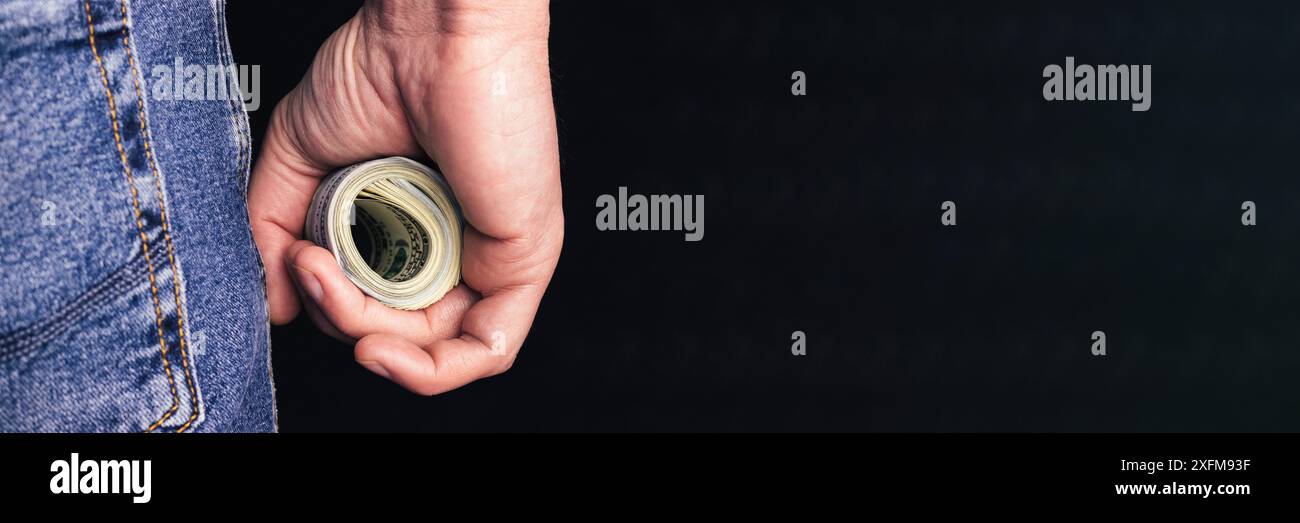 Male hand holding rolled-up money on dark background banner. Panoramic ...