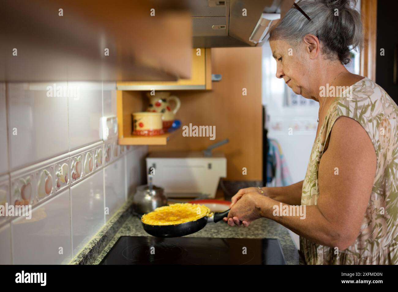 Elderly woman cooking a Spanish tortilla in a pan on the stove ...