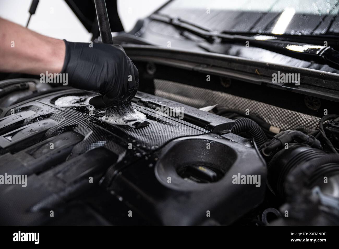 Mechanic wearing black gloves cleaning a car engine in a detailing ...