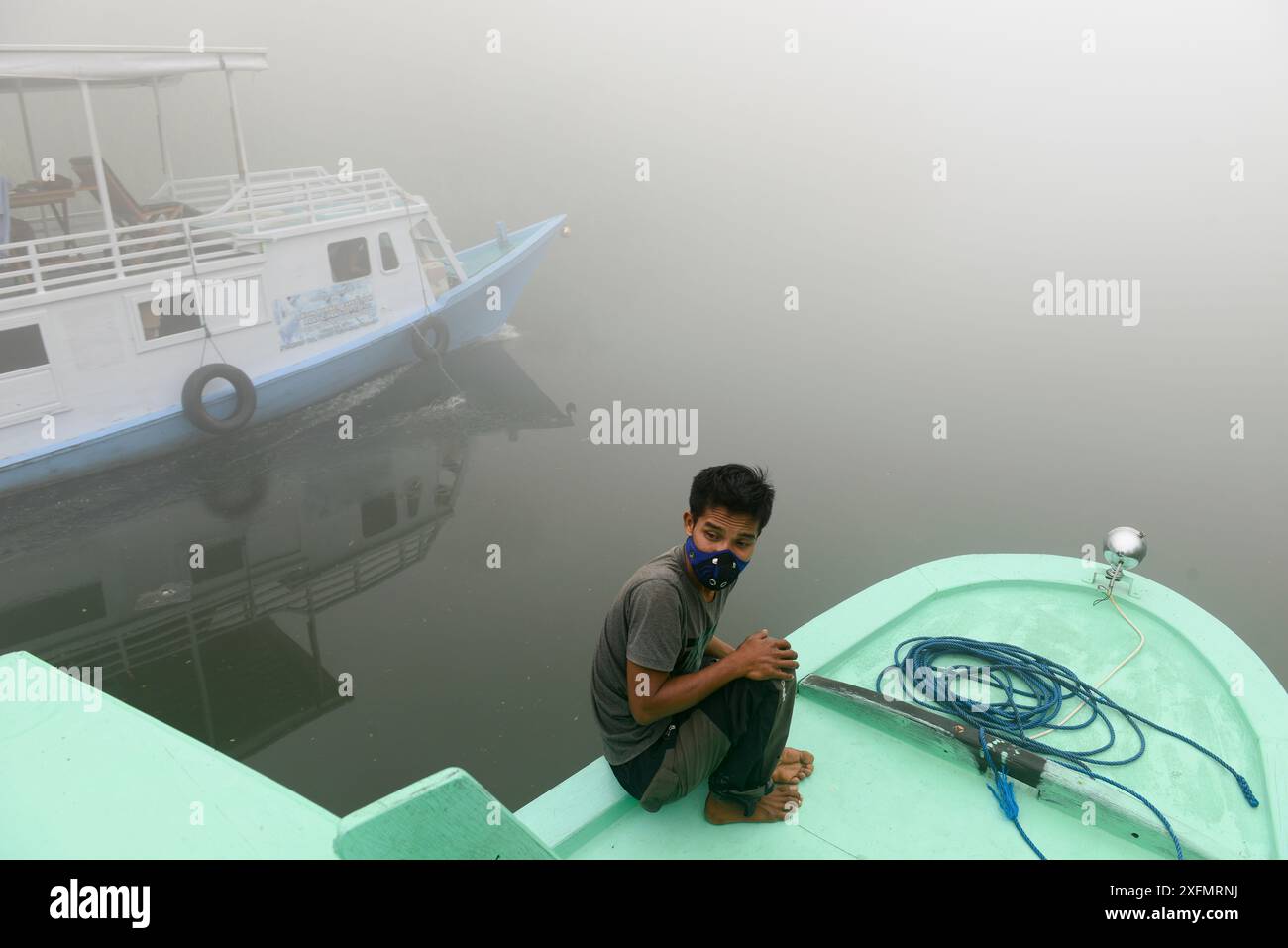 Man wearing an anti-pollution mask on a boat on the River Kumai ...