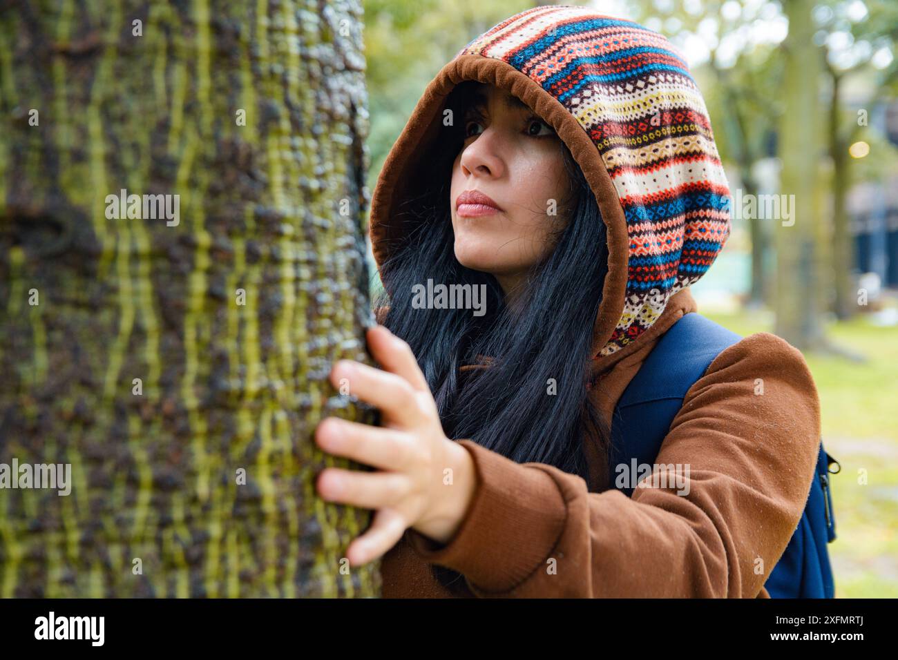 young woman standing touching a tree with concern, she is feeling pain ...