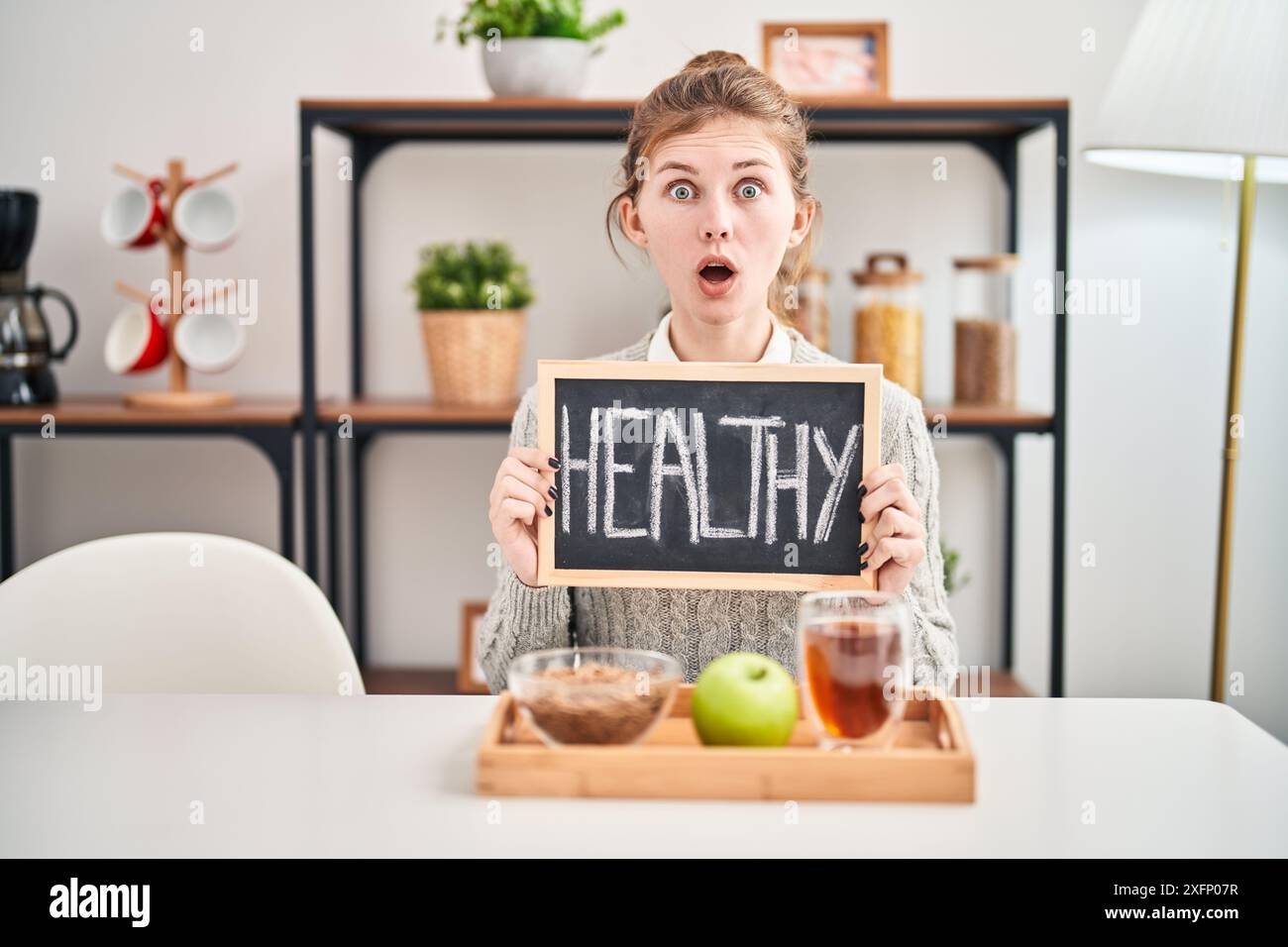 Shocked expression crosses the face of young, blonde woman at home, fear and amazement mingled ...