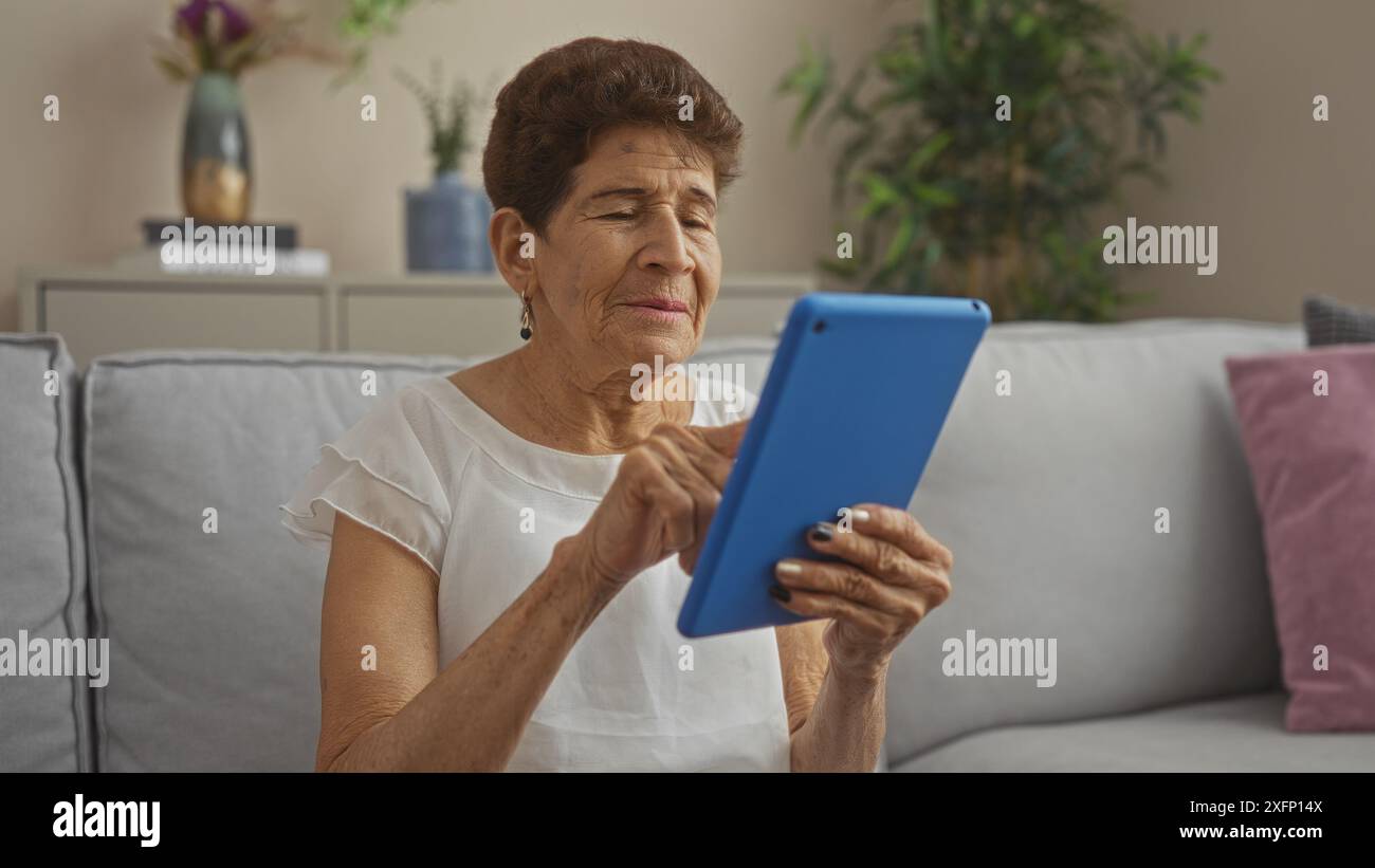 Elderly hispanic woman with short hair using a blue tablet indoors on a ...