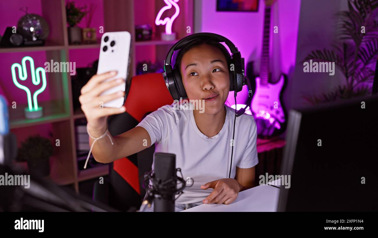 A young asian woman takes a selfie in a vibrant gaming room with neon ...