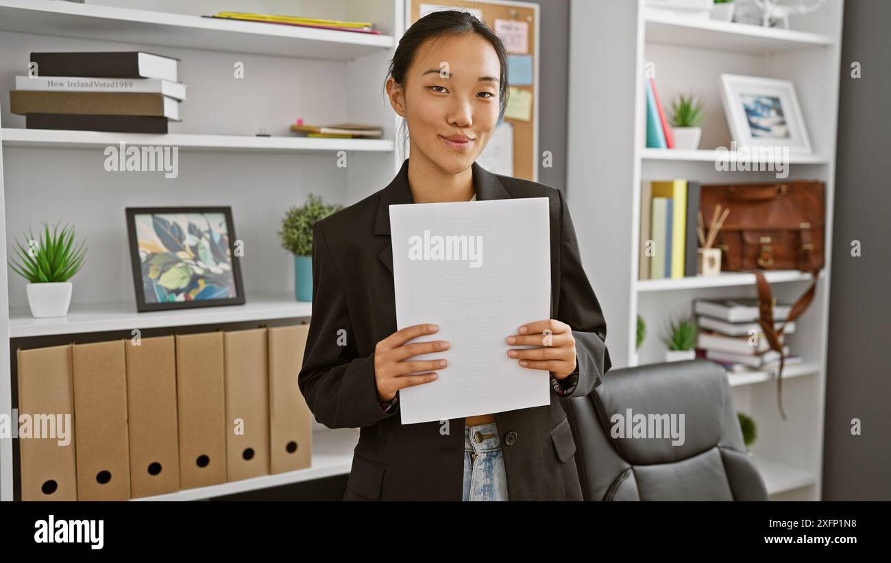 A professional asian woman holds a document in a modern office setting ...