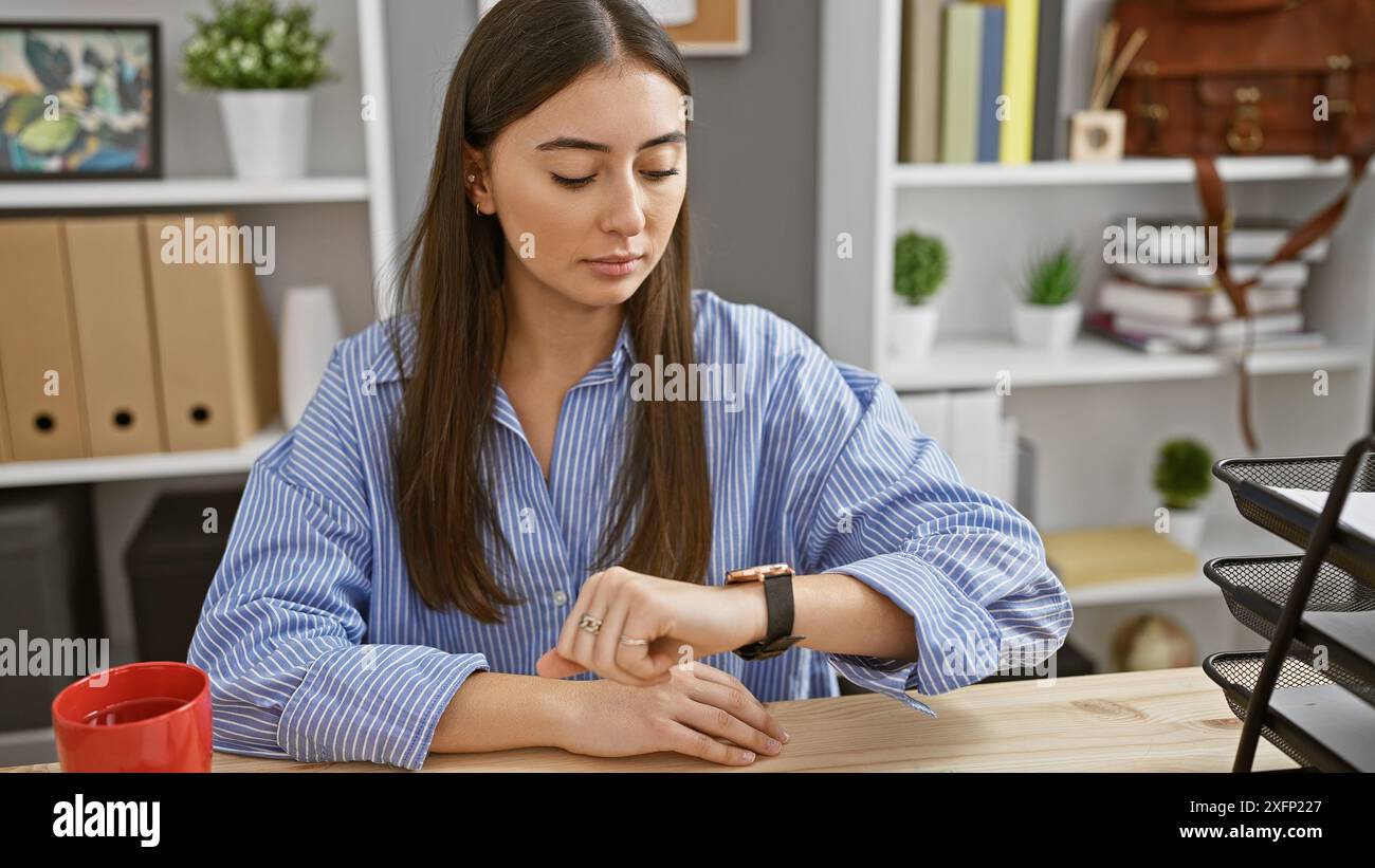 A young hispanic woman checks the time on her watch in a modern office ...