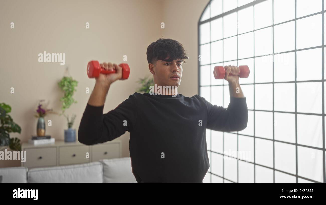 Handsome young hispanic man lifting red dumbbells in a modern living ...