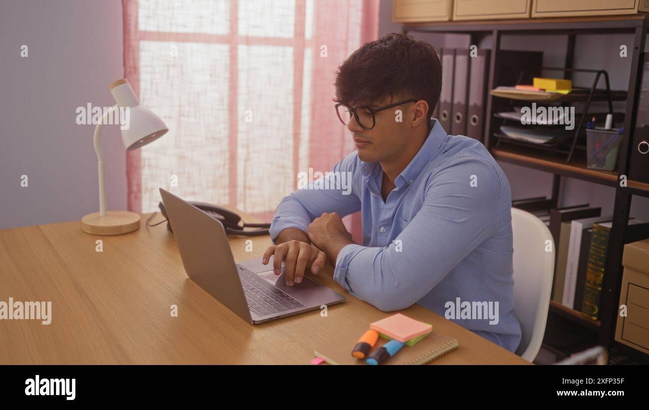 Handsome hispanic man working on a laptop in an office setting with ...