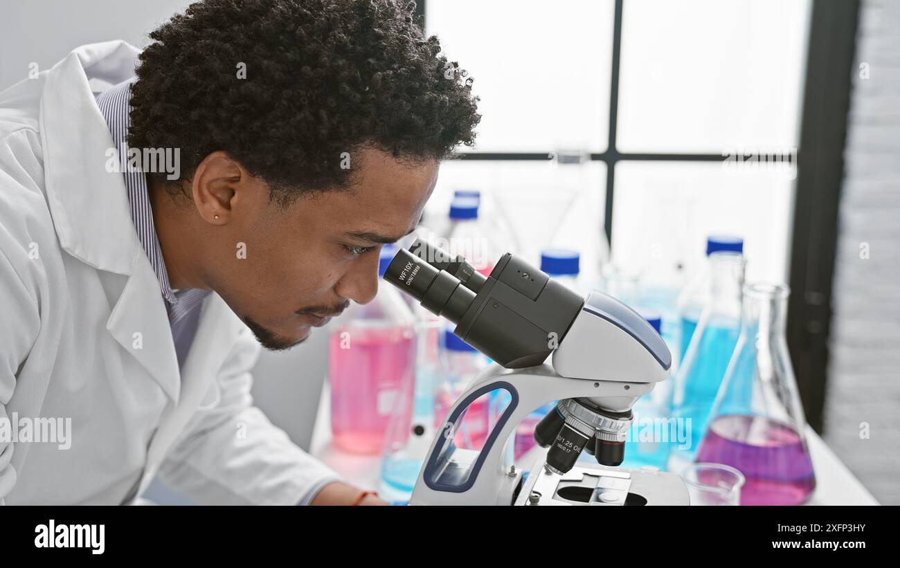 Handsome man analyzing samples under microscope in a modern laboratory ...