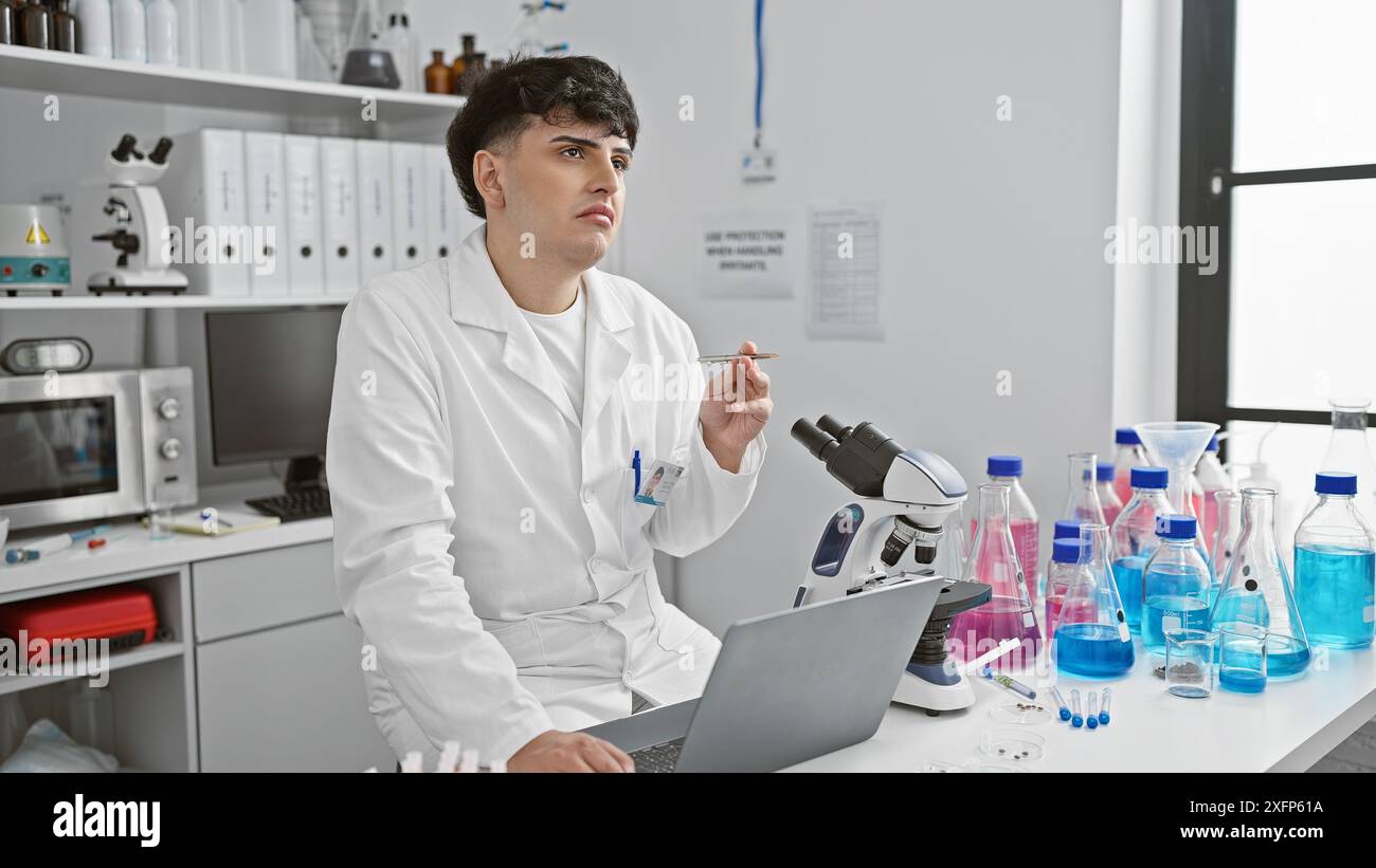 Young man in lab coat pondering a test tube in a modern laboratory with ...
