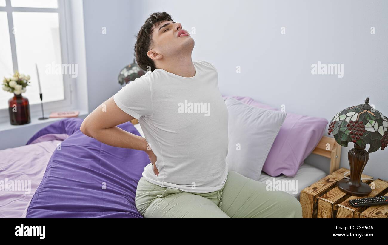 A man expressing back pain while sitting on the bed in a modern bedroom ...