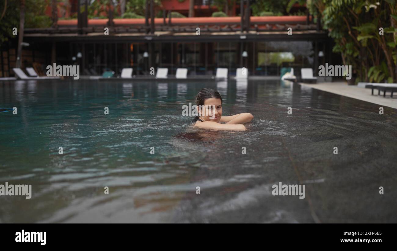 A serene woman relaxing in an expansive outdoor swimming pool at a ...