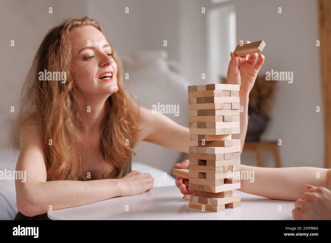 two women playing Jenga board game at home, excitement and relaxation ...