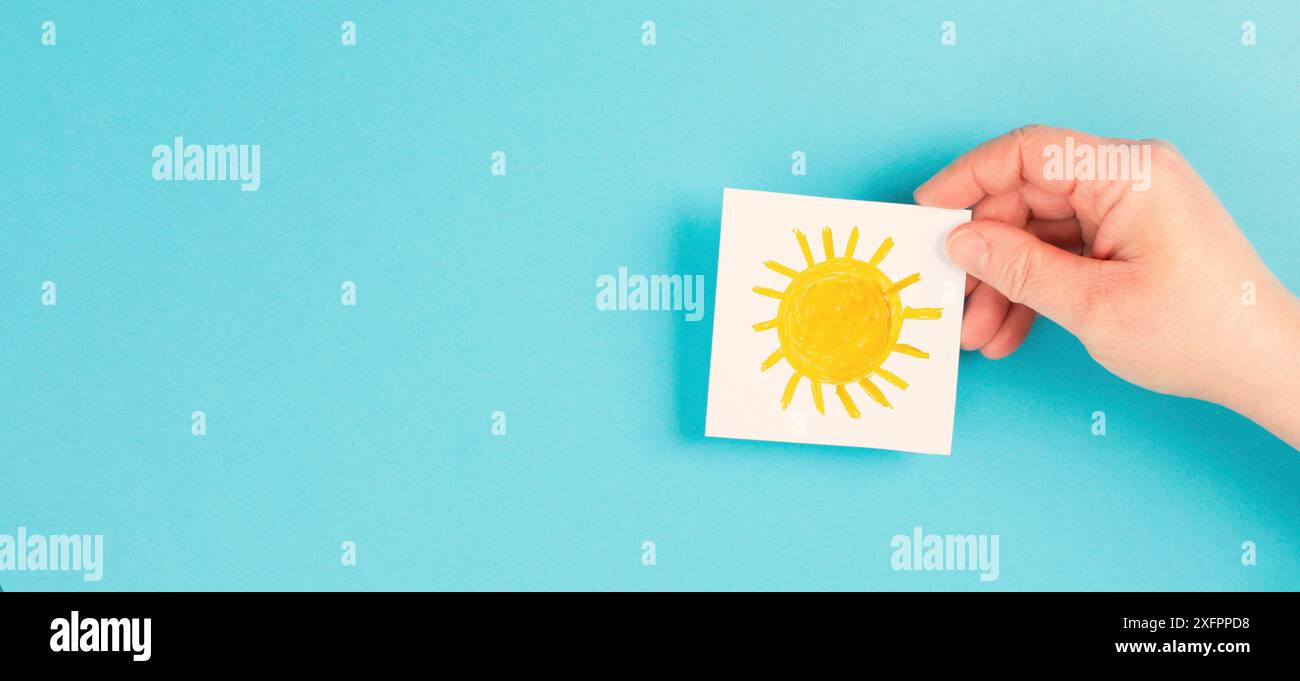 Holding a paper with a yellow sun, hot temperture on a summer day ...
