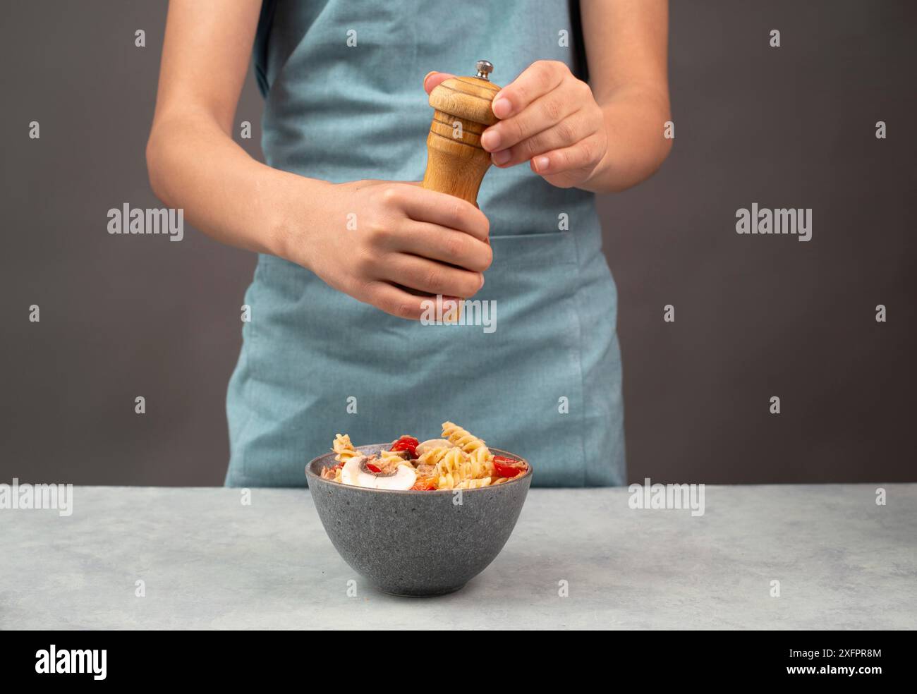 Putting pepper in a pasta salad, sliced mushroom, tomato, red pepper ...