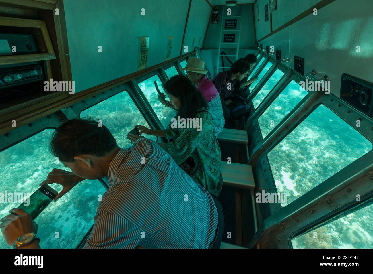 Tourists in a glass bottom boat looking at corals around the shallow ...
