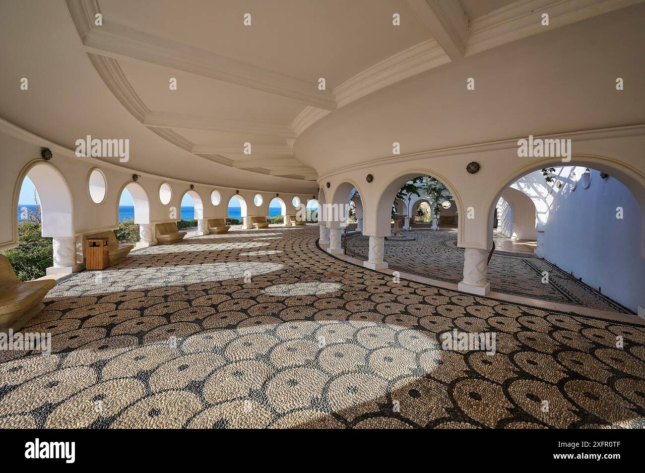 Interior of a circular building with open arches and a view of the sea ...