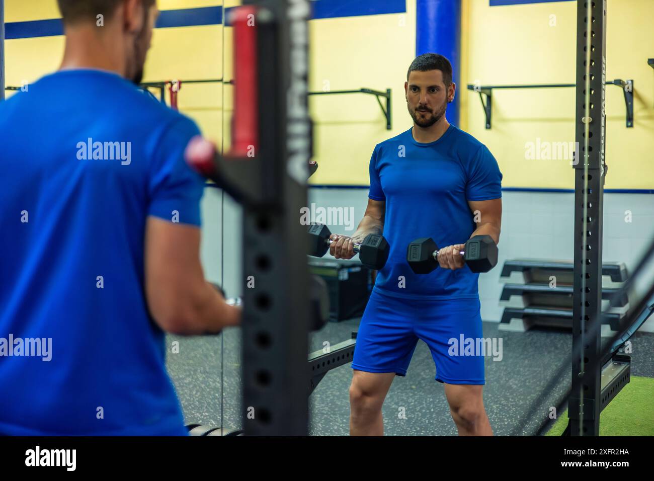 young fitness athlete performs bicep exercises with dumbbells, his ...